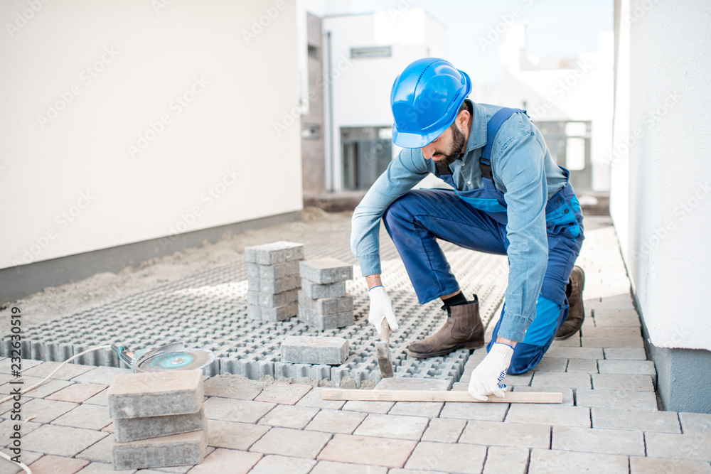 Builder in uniform laying paving tiles on the construction site with ...