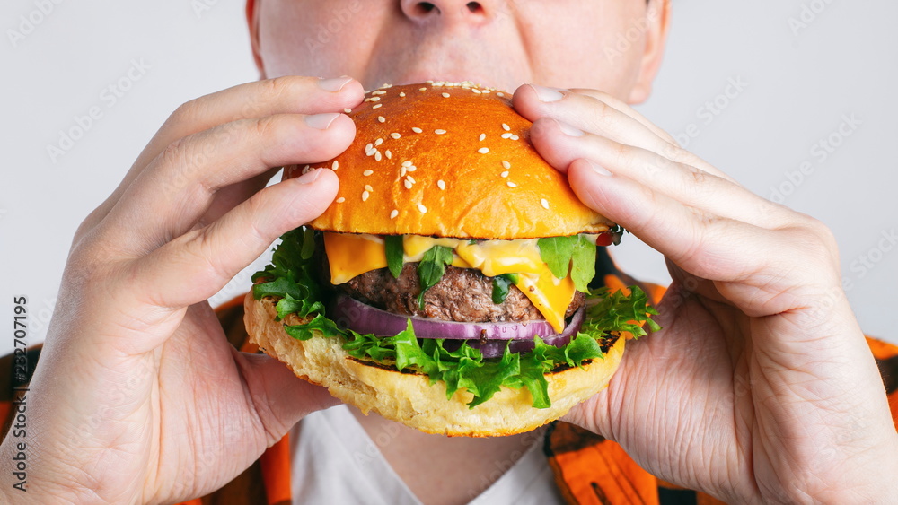 A young guy is holding a fresh Burger. A very hungry student eats fast ...