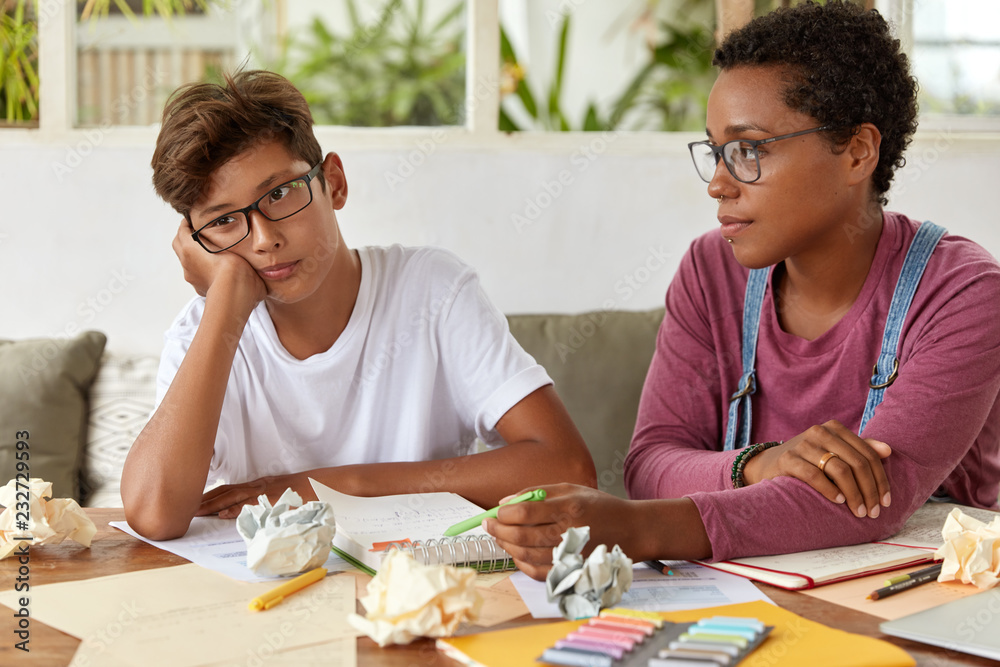 Multiracial teenagers do homework together, sit together at desktop ...
