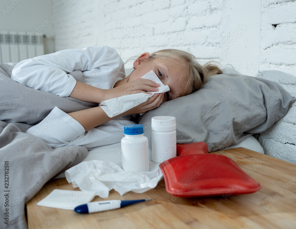 Little girl lying sick in bed blowing her nose feeling sick with high ...
