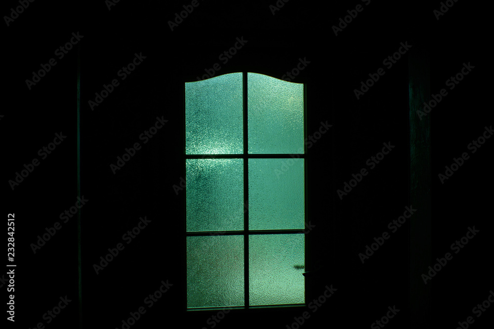 Dark silhouette of glass door in supernatural green light. Locked alone ...