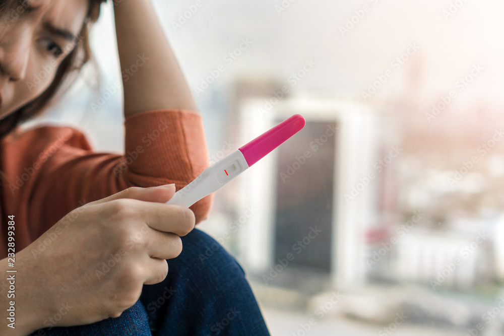 Unhappy young asian woman holding pregnancy test showing a negative ...