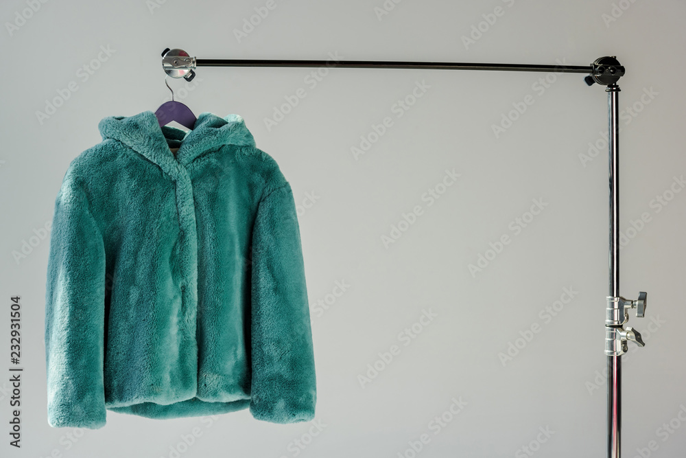 fluffy green faux fur coat hanging on rack at grey background with ...