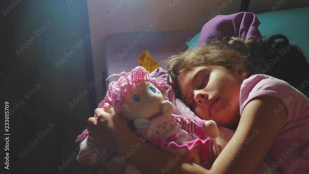 Adorable little girl sleep in the sofa bed and hug her baby doll ...