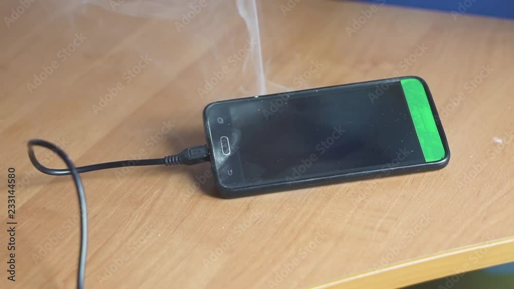 Smartphone is lying on the table and smoking and burning. Soon the fire ...