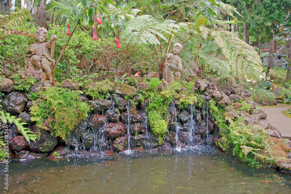 Small waterfall with statues in park. Statues of two boys decorate a ...