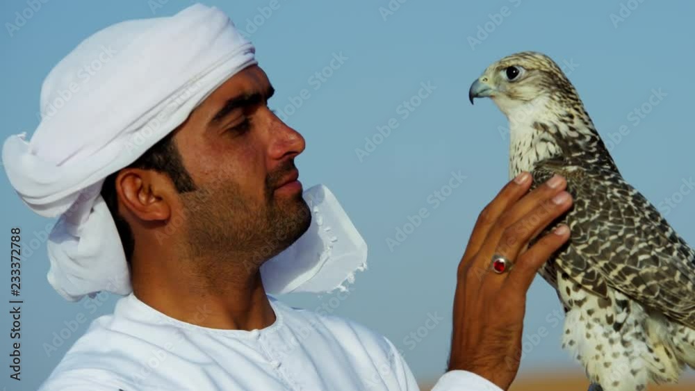 Trained falcon tethered to male owner wearing traditional Arabic dress ...
