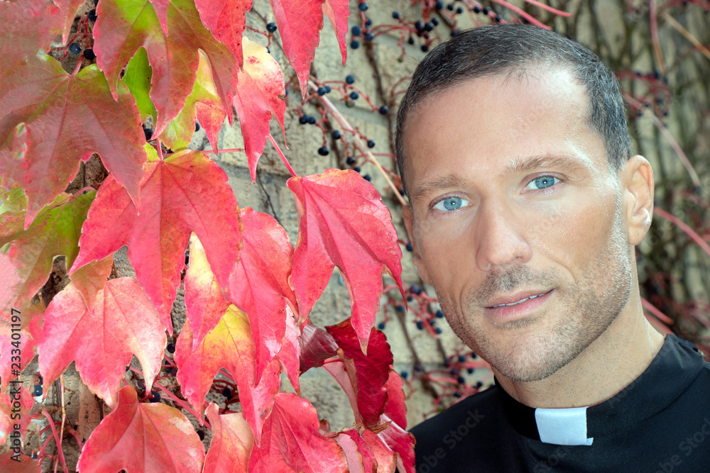 Good looking priest with visible collar poses for portrait next to red ...