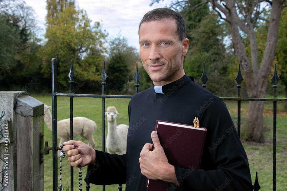 Poster Good looking priest standing next to iron gate holding bible ...
