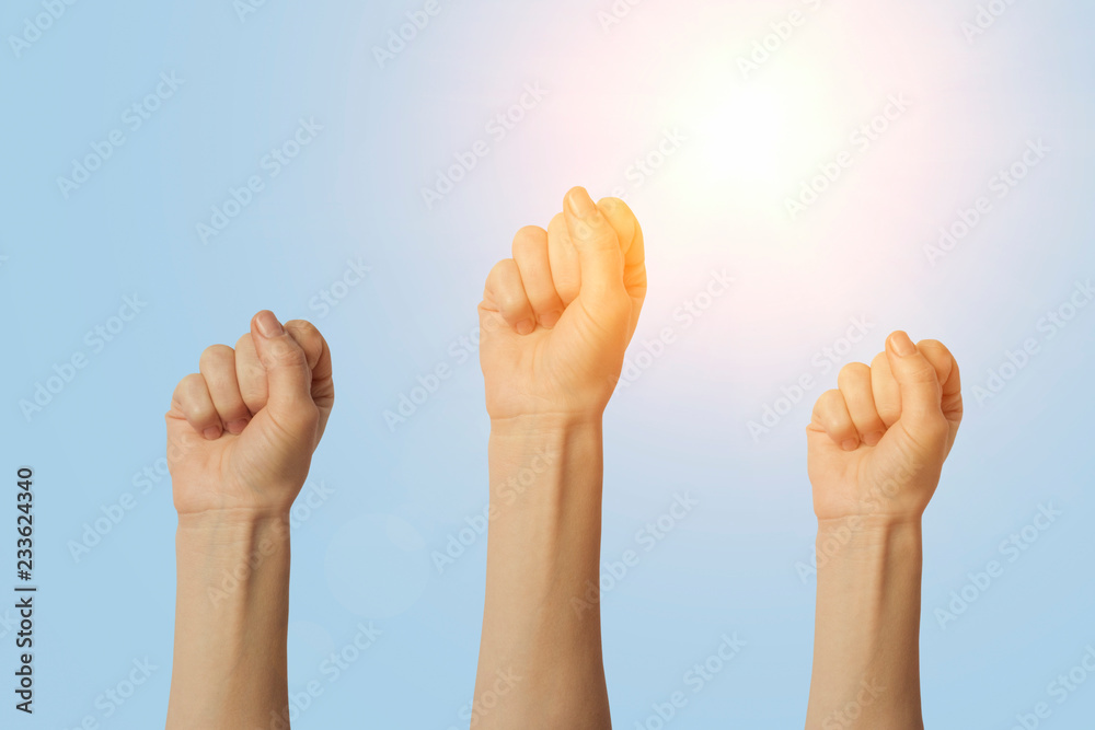 Female hands clenched into a fist and raised up on a blue background ...