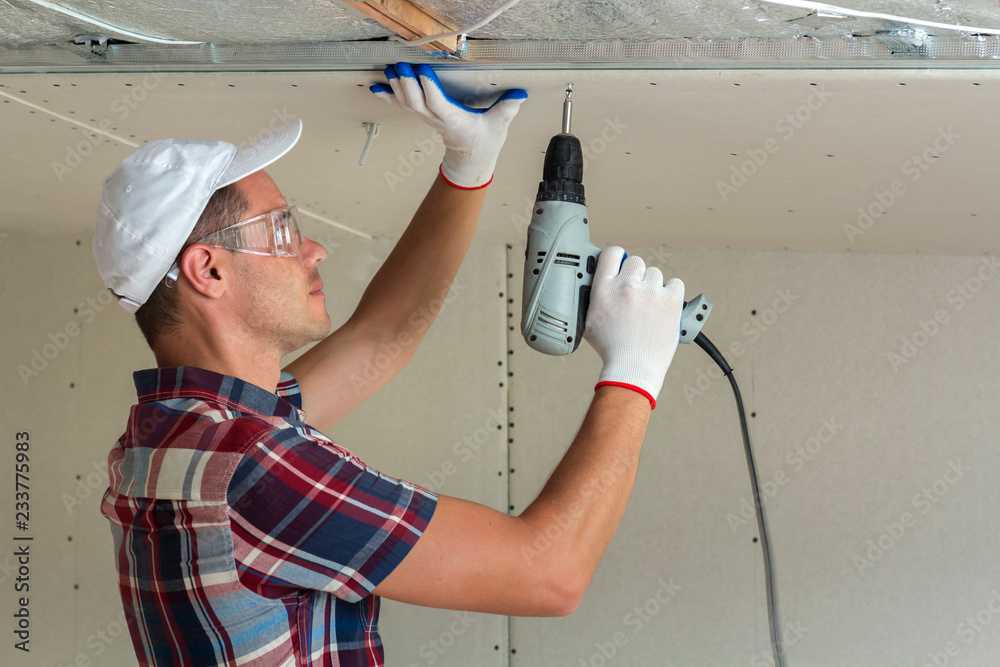 Young man in goggles fixing drywall suspended ceiling to metal frame ...