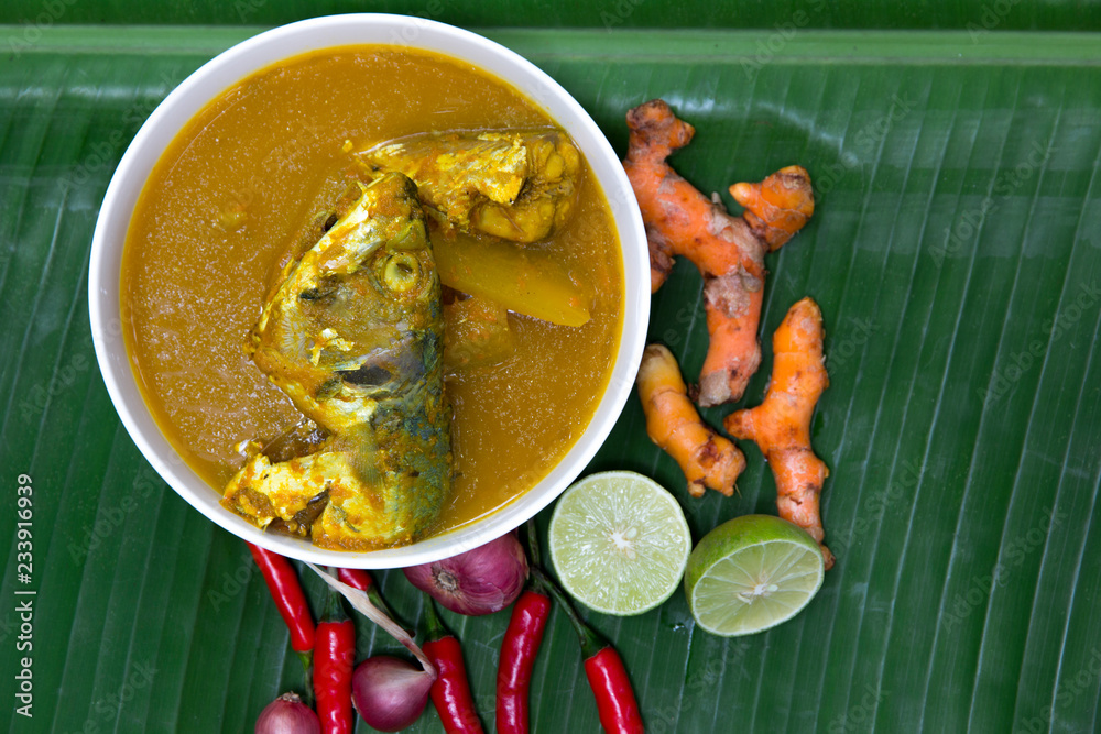 Sour spicy yellow soup with fresh sea fish in white bowl on banana leaf ...