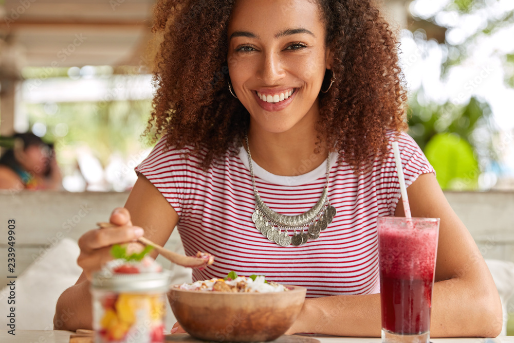 Pretty young female model holds wooden spoon, tastes delicious exotic ...