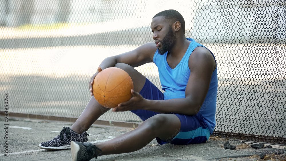 Lonely black basketball player sitting on stadium ground and holding ...