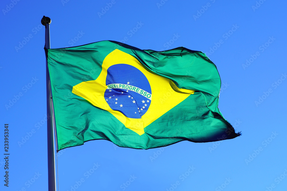 Flag of Brazil waving in the wind in front of a blue sky, isolated and ...