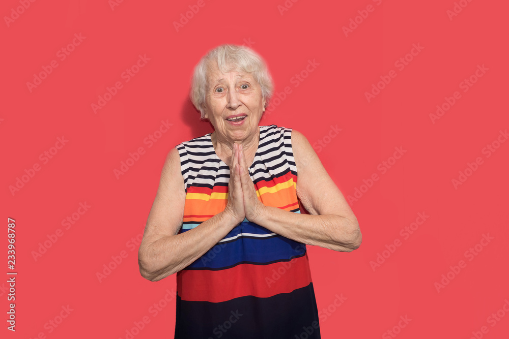 Old smiling woman with surprised expression on her face on red studio ...