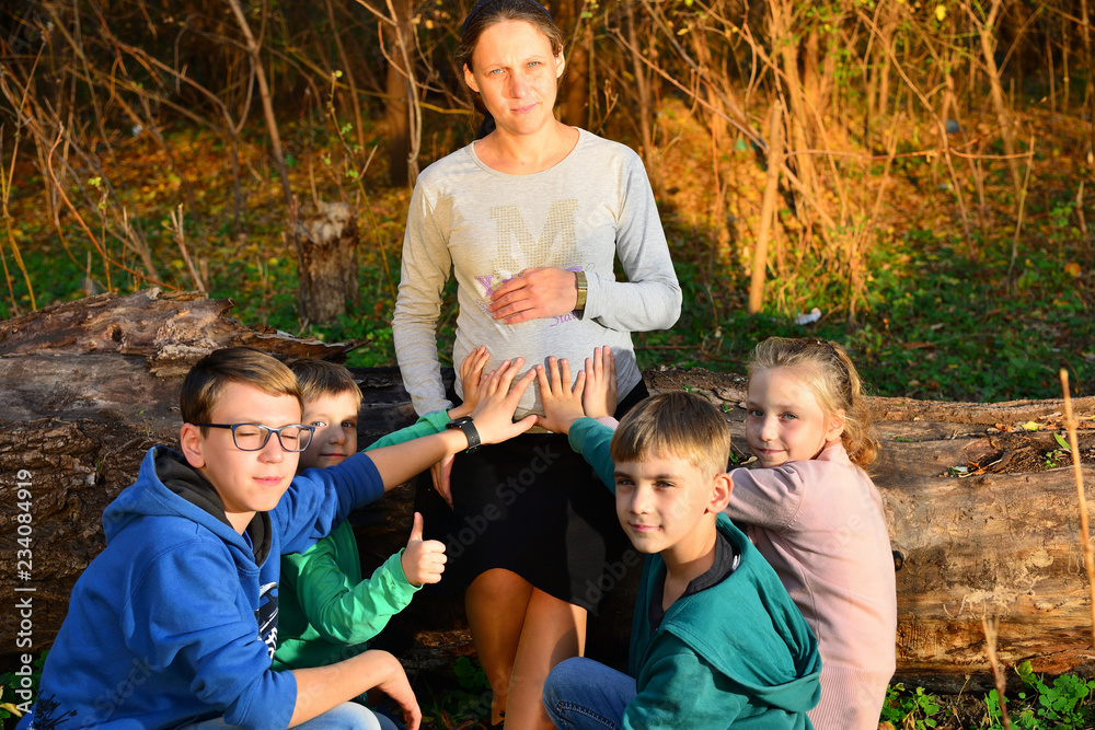 Young children sit next to a pregnant woman and hold their hands on ...