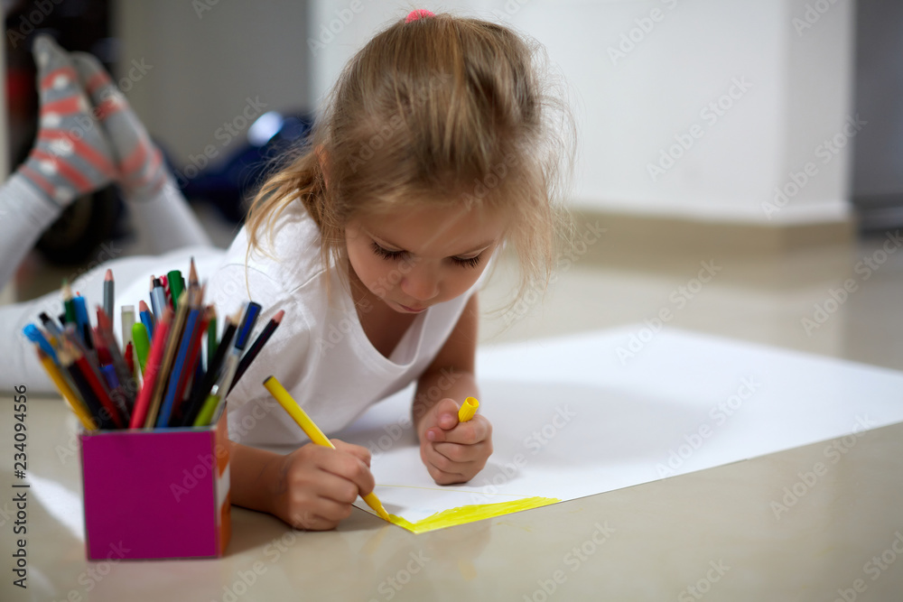Adorable little girl lying on floor and drawing on huge paper sheet ...