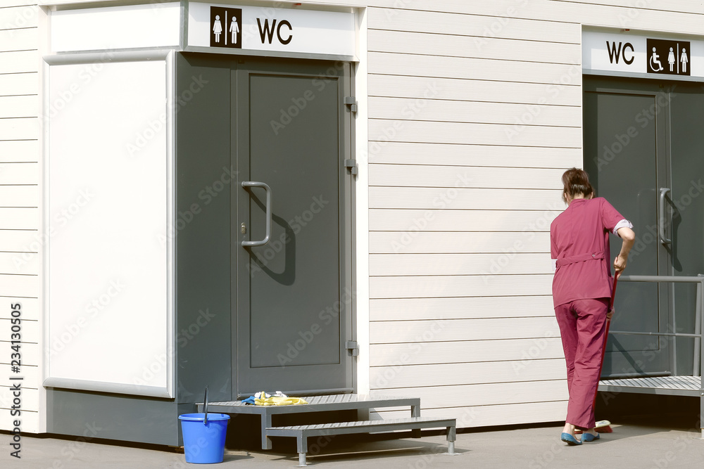 woman worker in red uniform cleans outdoor public restroom at city park ...