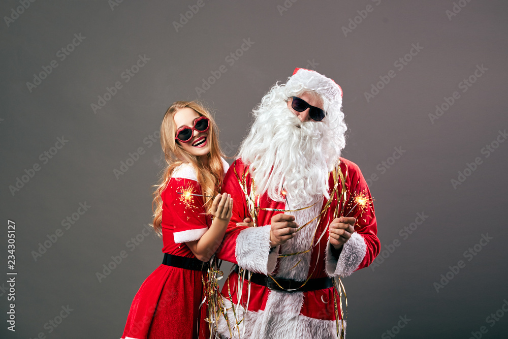Santa Claus and young beautiful mrs. Claus in sunglasses are holding ...