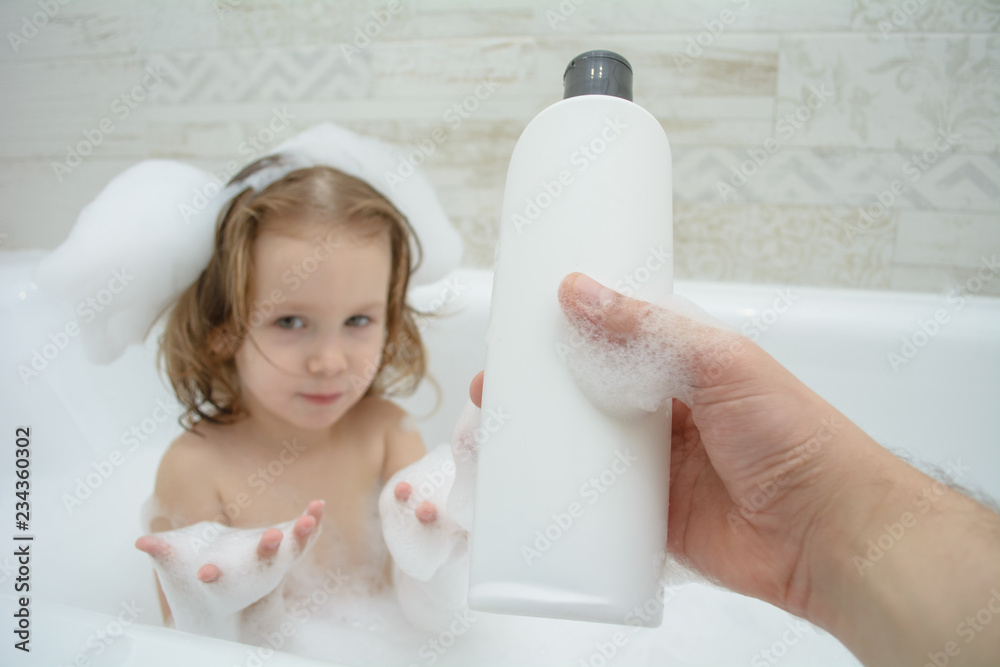 Parent gives a plastic bottle of shampoos to a beautiful child sitting ...