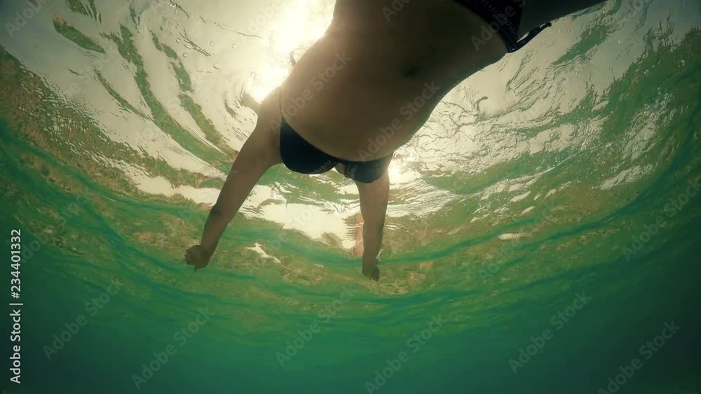 Following a woman swimming in pool, underwater view with sunset sun ...