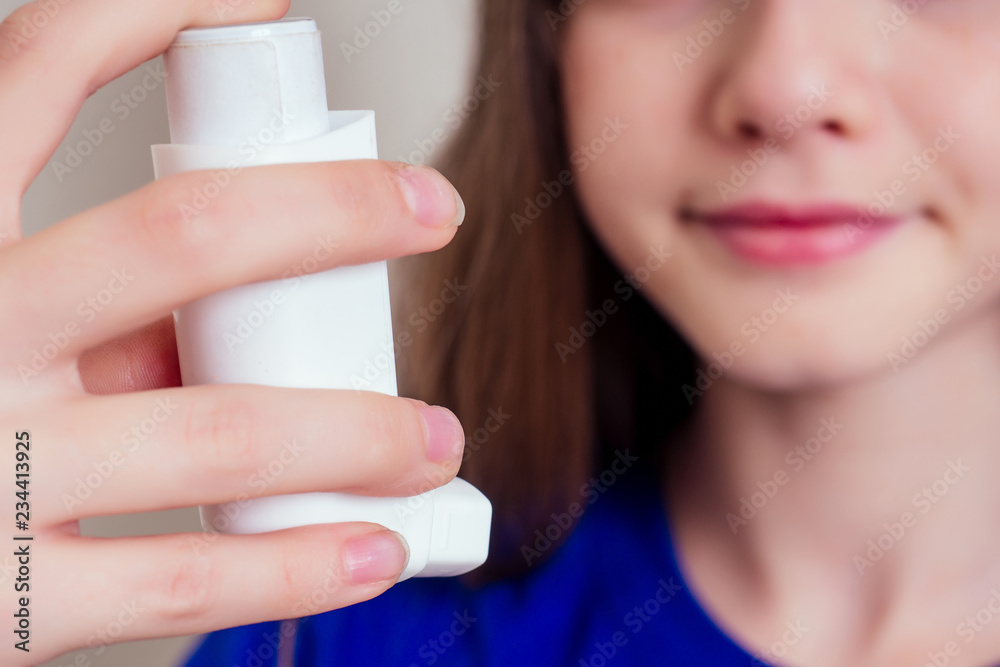 Young teen girl woman using asthma inhaler at home against a white wall ...