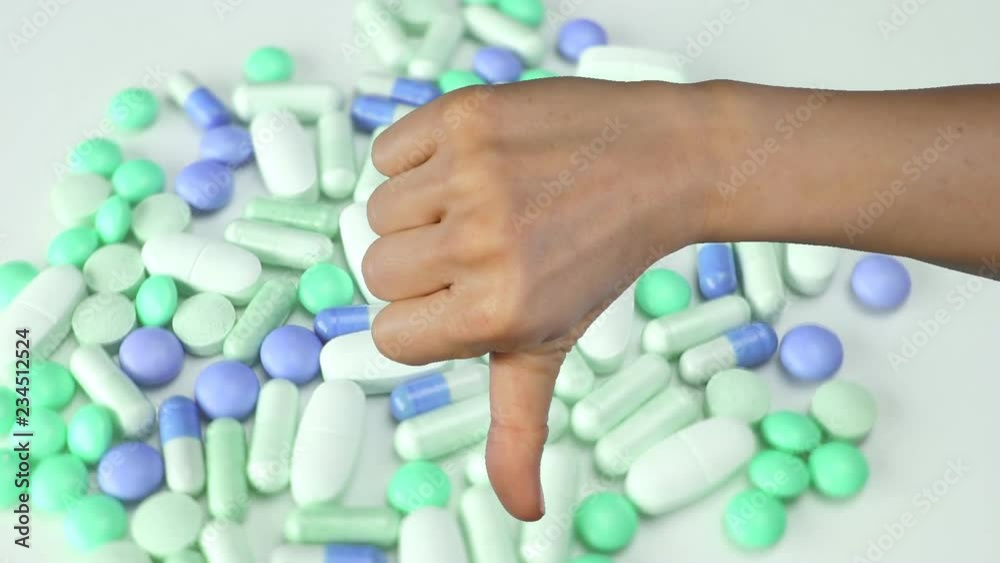 Female hand goes from thumbs up to thumbs down. Medical pill background ...