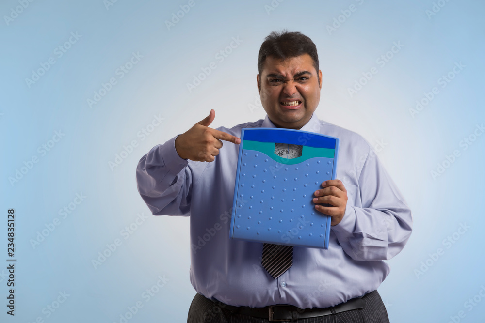 Frustrated obese man in formal clothes holding weighing scale in one ...
