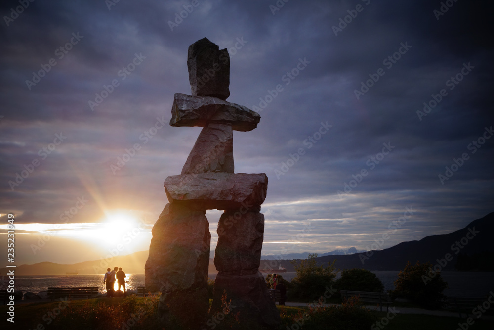 Silhouette of people watching the sunset near the Inuksuk Inuit rock ...
