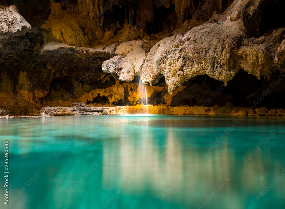A small picturesque waterfall in a cave falls into a warm blue and ...