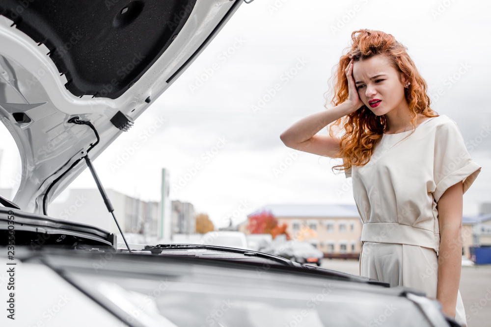 Redhead woman under the hood of the car, try to fix the car engine ...