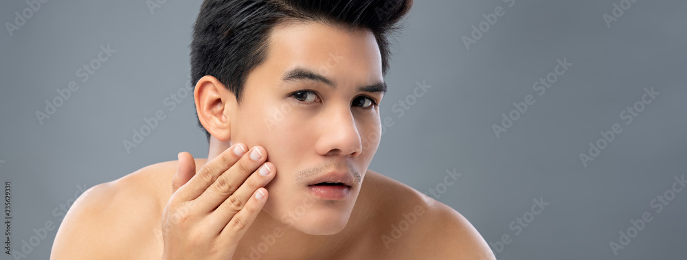 Portrait of shirtless young handsome Asian man checking his face skin ...