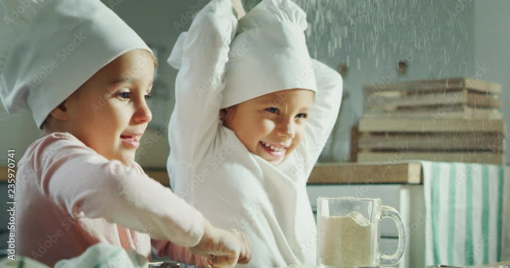 Portrait of two beautiful kids (sisters) in chef clothes while cooking ...