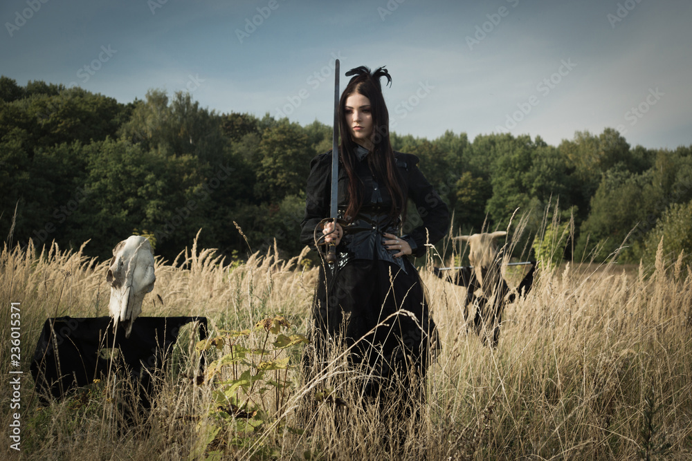 Gothic girl with a sword in her hands next to the skull of a cow on a ...