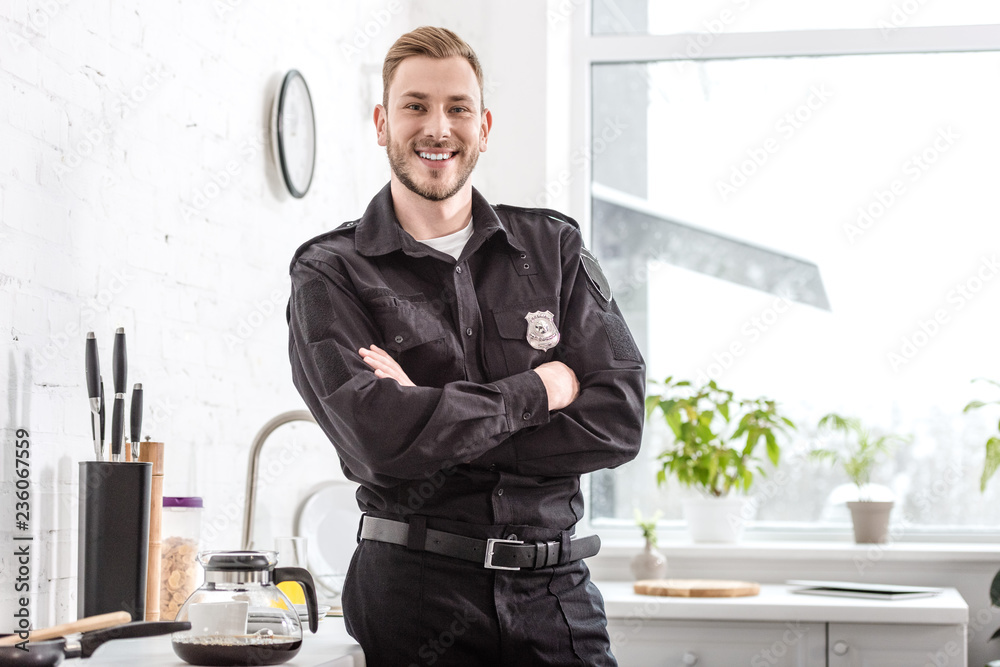 Smiling police officer with crossed arms standing next to kitchen table ...
