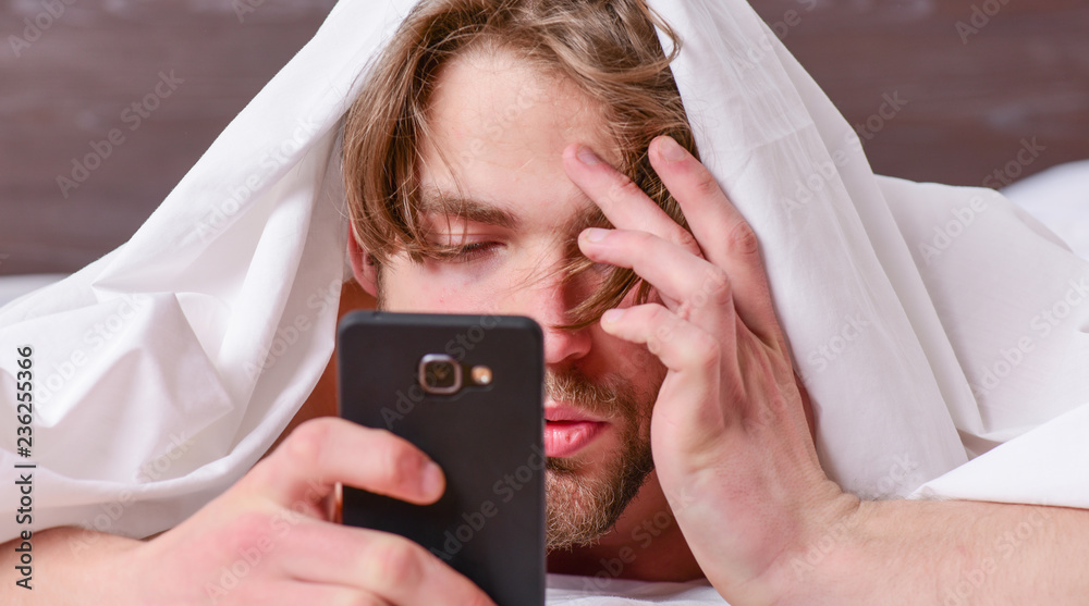 Handsome man using clock in bed after waking up in the morning. A young ...