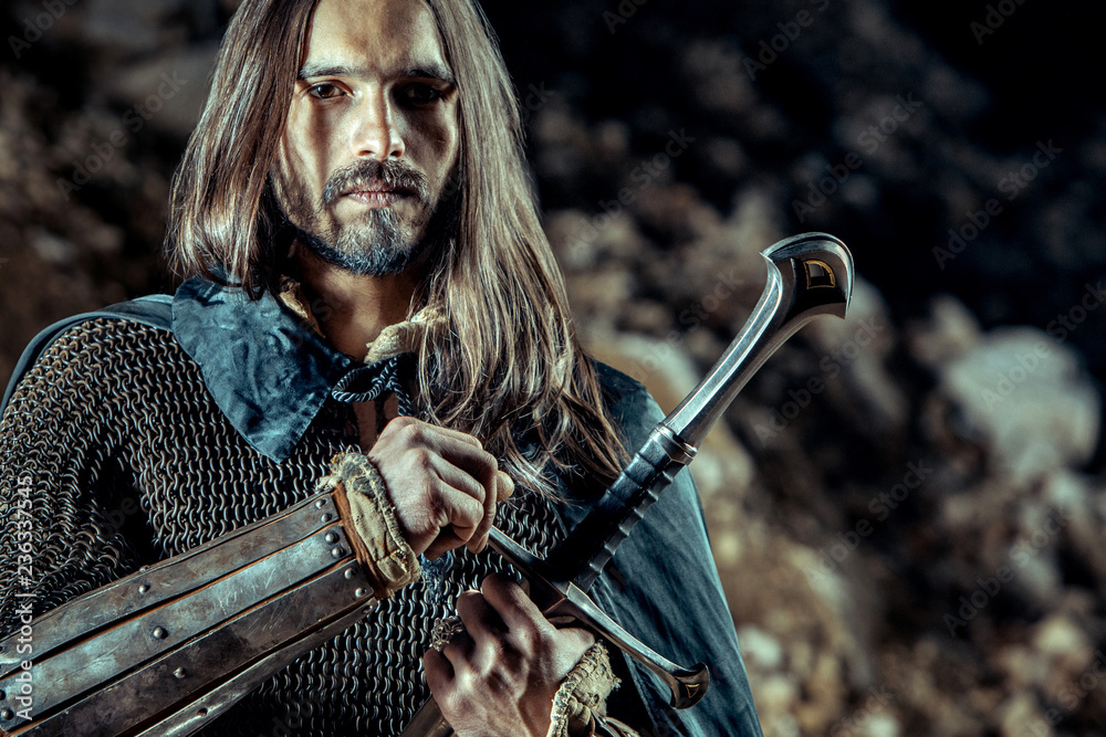Long haired knight with the two-handed sword. Rocks on the background ...