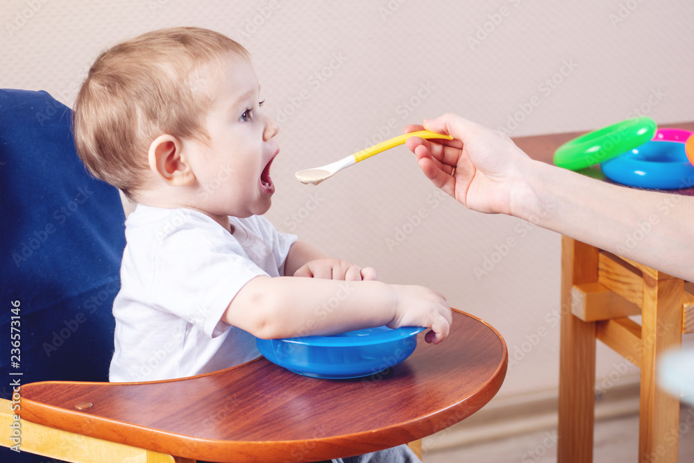 Cute baby eating opening his mouth wide sitting on a chair in the ...