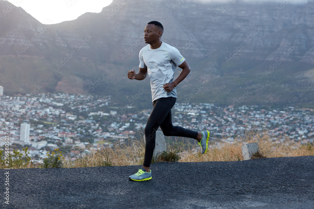 Outside shot of sporty dark skinned man in casual clothing, runs ...