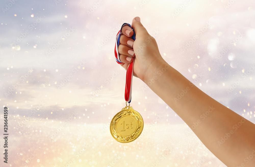 woman hand raised, holding gold medal against glitter background. award ...