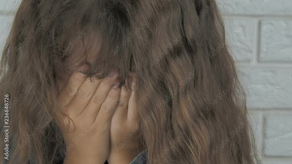 A depressed child hides face with hands. Little girl crying covering ...