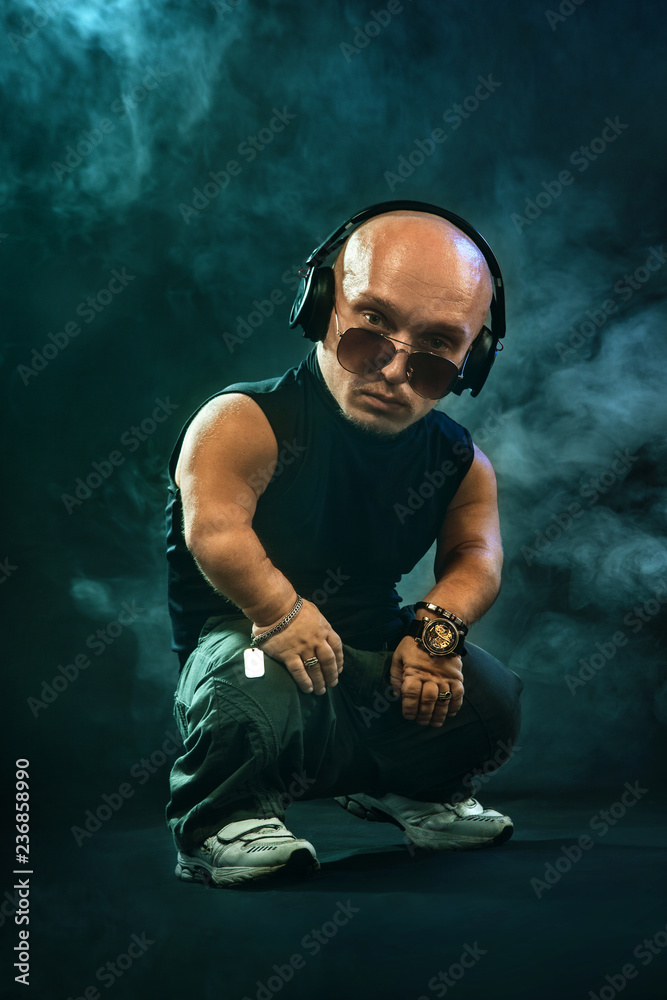 Portrait of stylish midget MC in with headphones and sunglasses posing ...