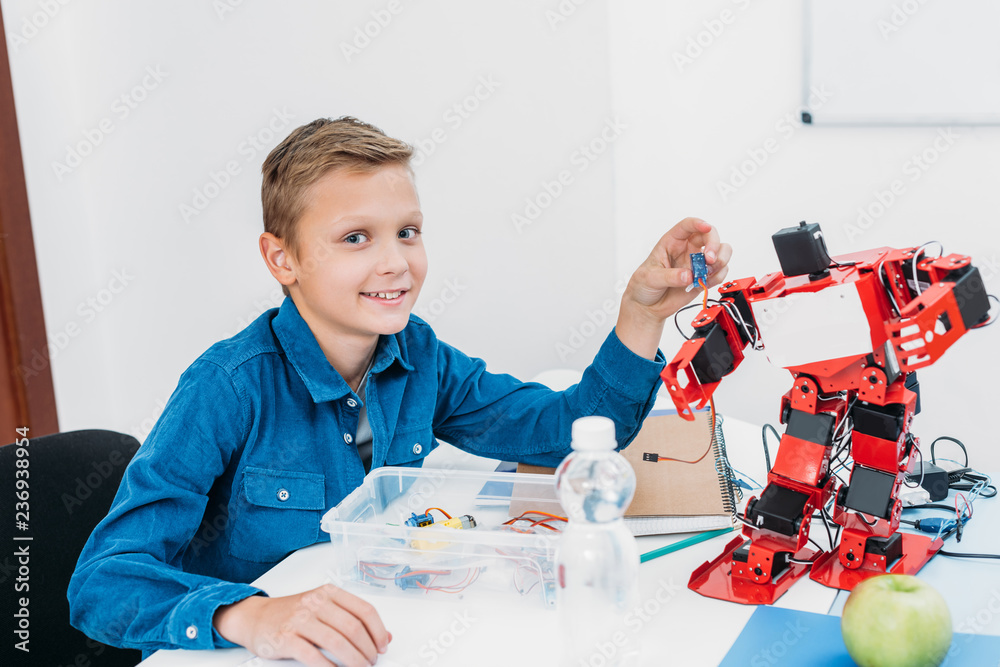 schoolboy sitting at table with robot model at STEM classroom and ...