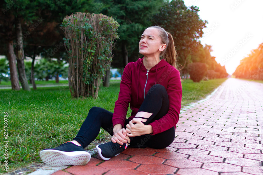 A young, fitness girl in sneakers and sportswear was injured while ...