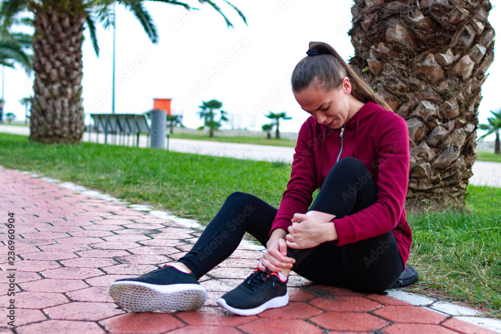A young, fitness girl in sneakers and sportswear was injured while ...