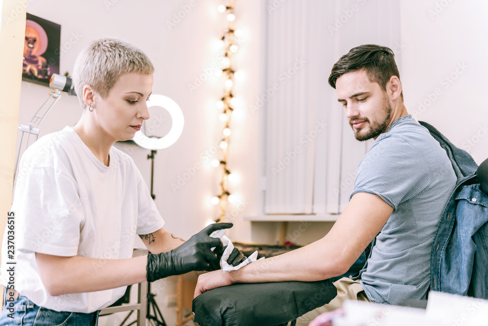 Good-looking tattoo master with boyish haircut wiping off area of bare ...