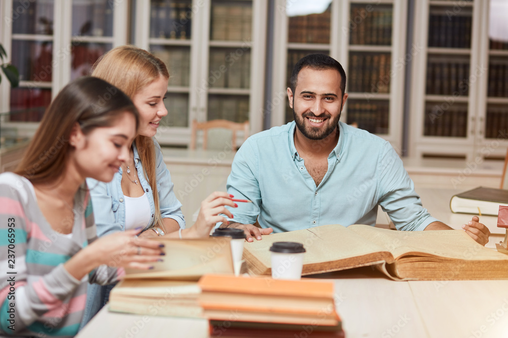 Happy young university students studying with books in library. Group ...
