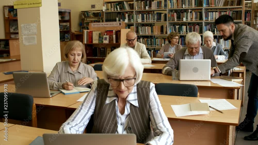 Group of elderly people sitting at desks in library or classroom and ...