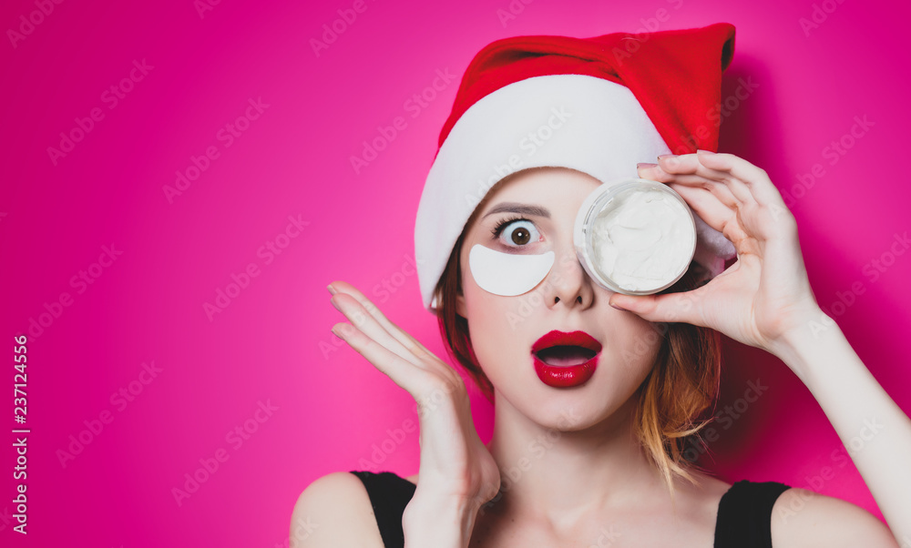 Woman using eye patch for her eyes in Santa Claus hat with cream on ...